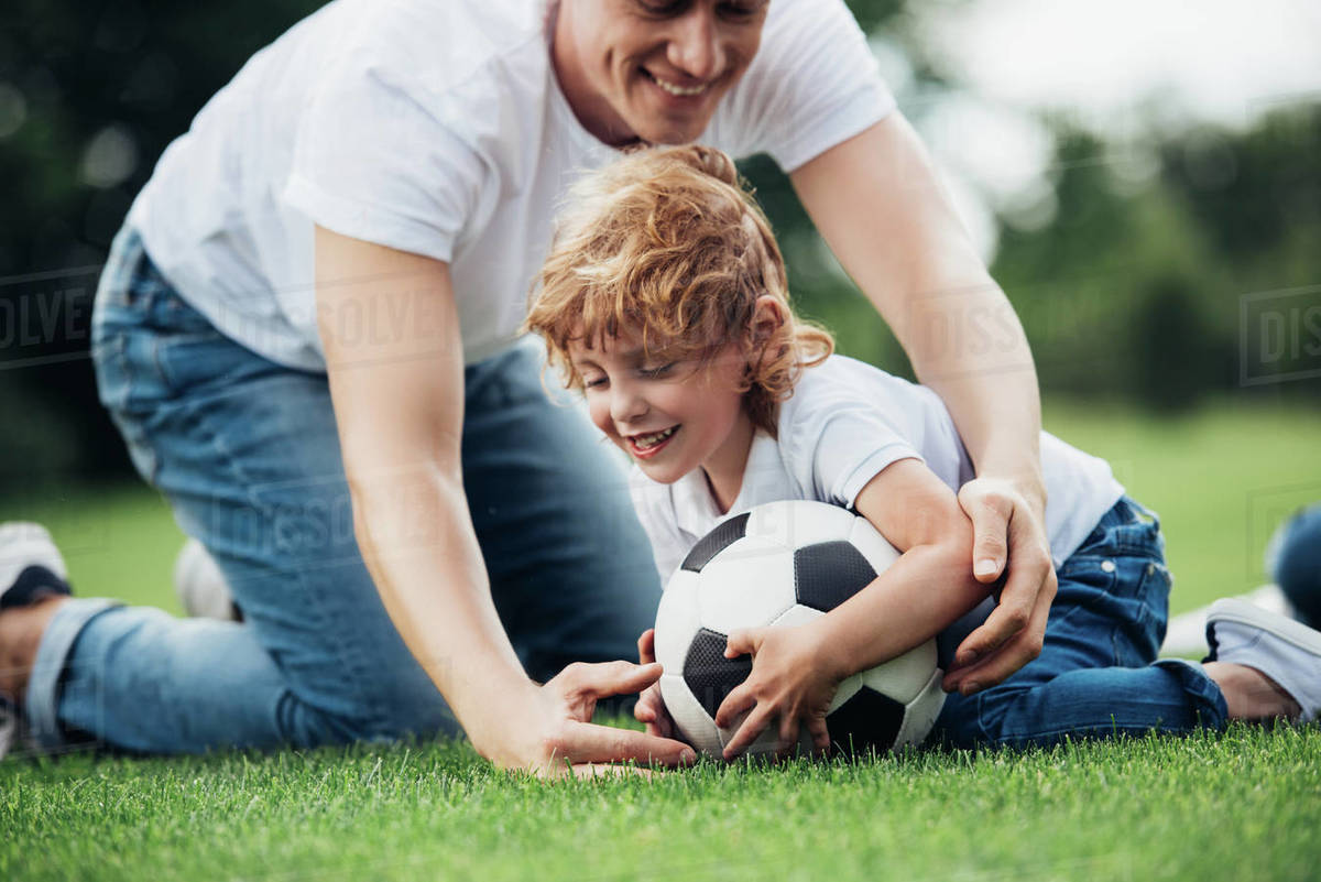 Happy father and son playing with soccer ball on green grass at park ...