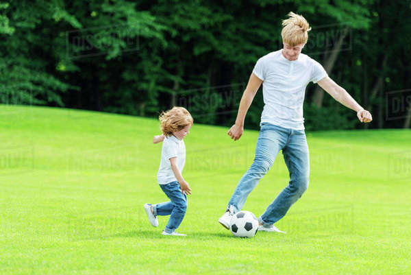 Happy father and son playing soccer on green grass in park - Royalty ...