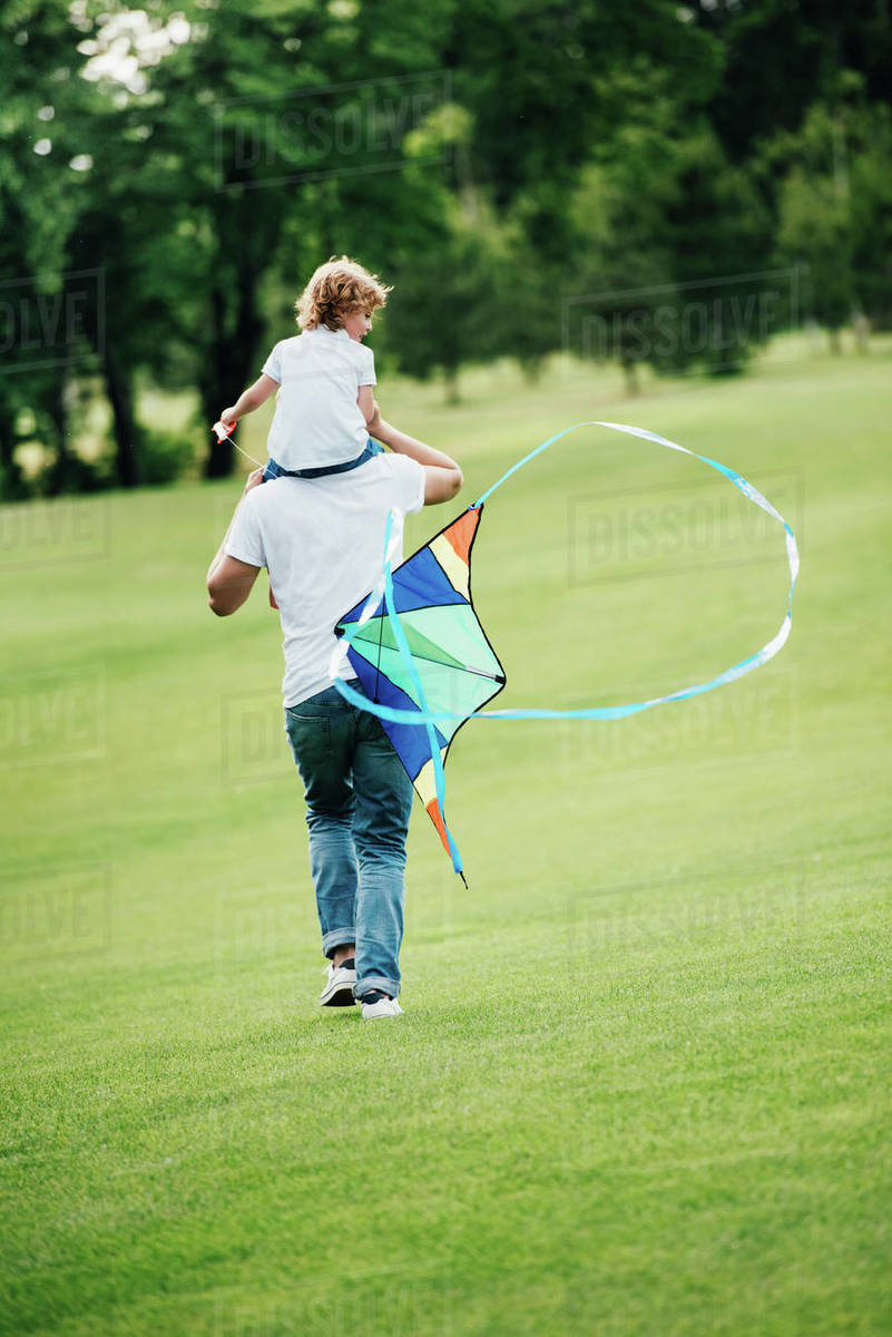 Back view of father carrying little son on shoulders while playing with ...