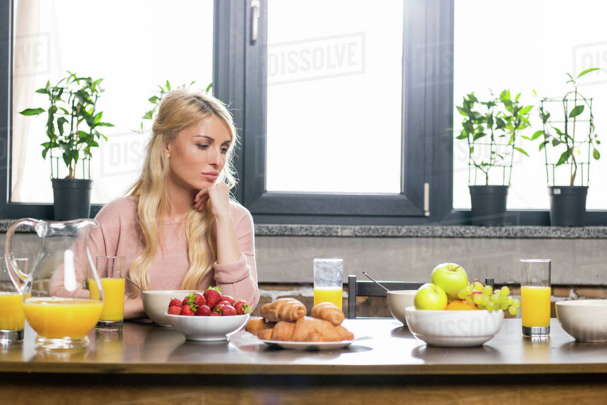 Pensive young woman sitting at table served for breakfast - Royalty ...
