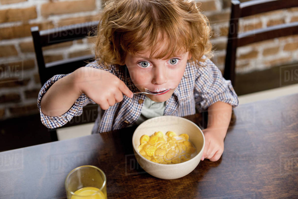 High angle view of cute little boy eating corn flakes for breakfast ...