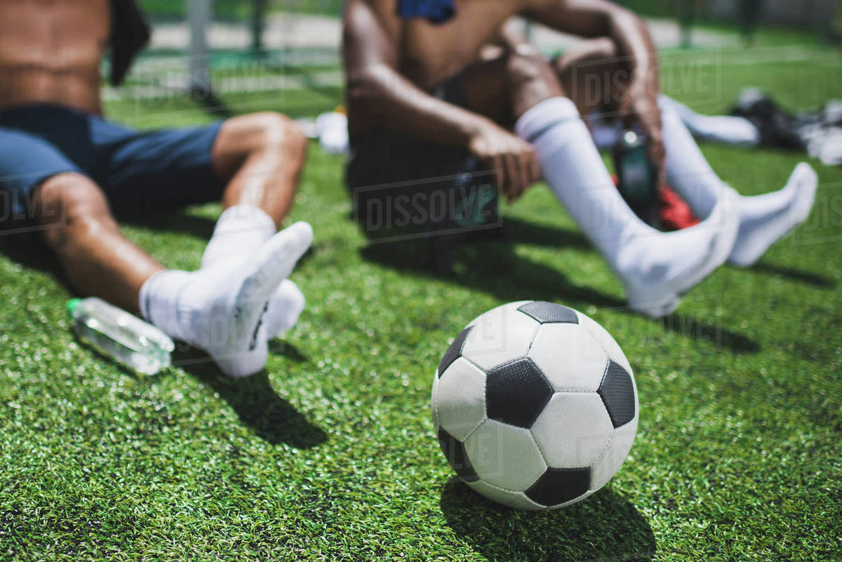 Soccer players resting on football field with soccer ball on foreground ...