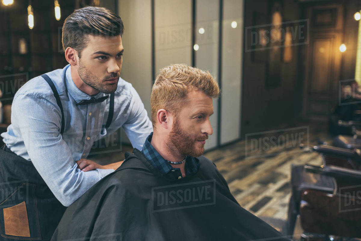 Stylish young barber standing behind customer that sitting in barber ...