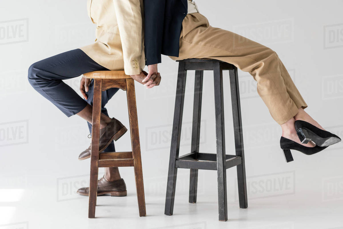 Cropped shot of multiethnic couple sitting back to back on stools and ...