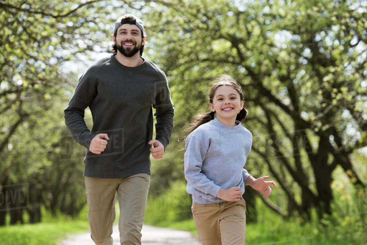 Smiling father and daughter running in park - Stock Photo - Dissolve