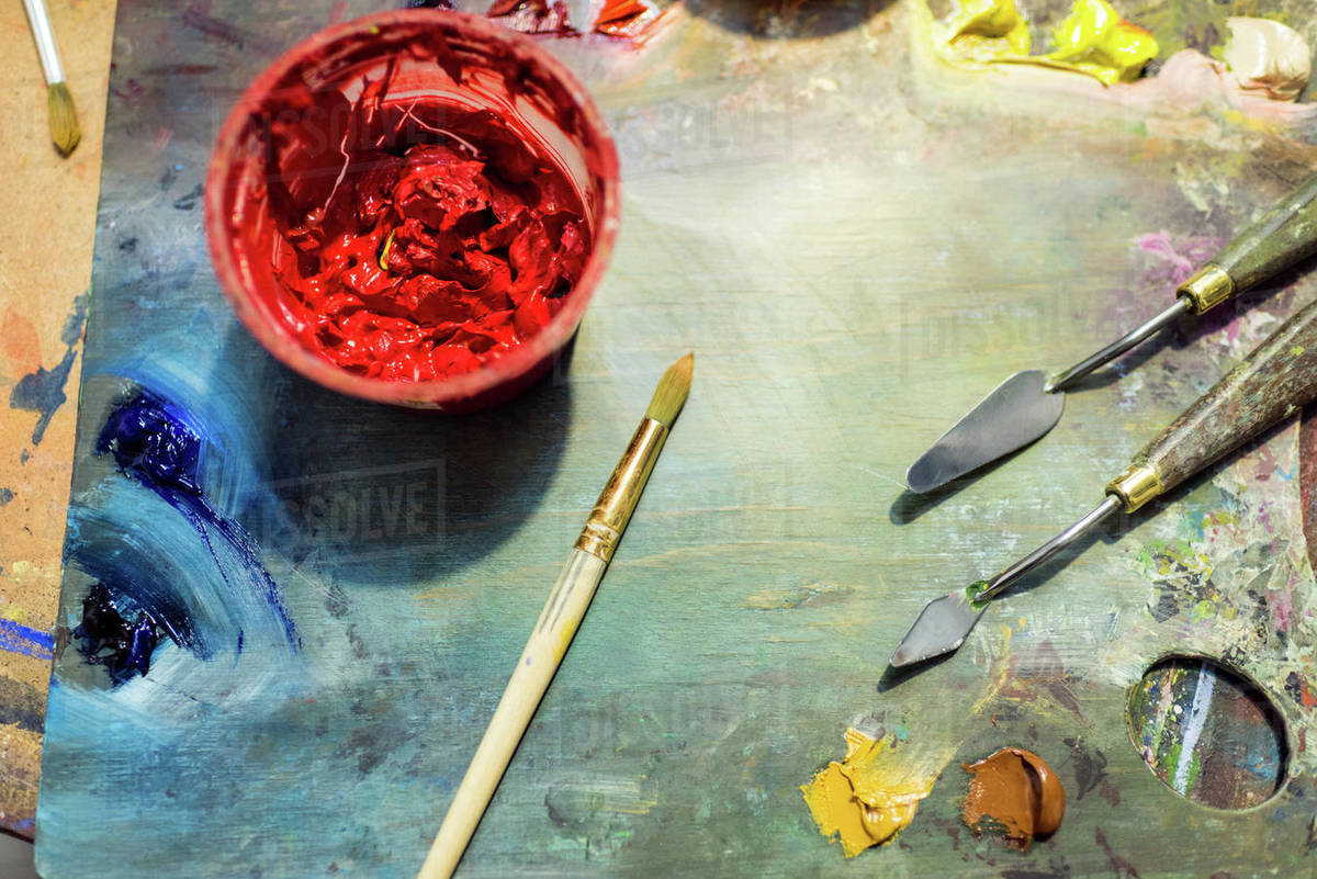 Painting brushes, palette and red poster paint on wooden table in ...