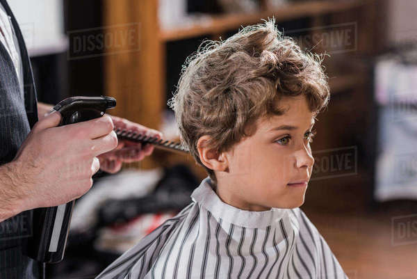 Cropped shot of barber spraying hair of adorable little kid at kids ...