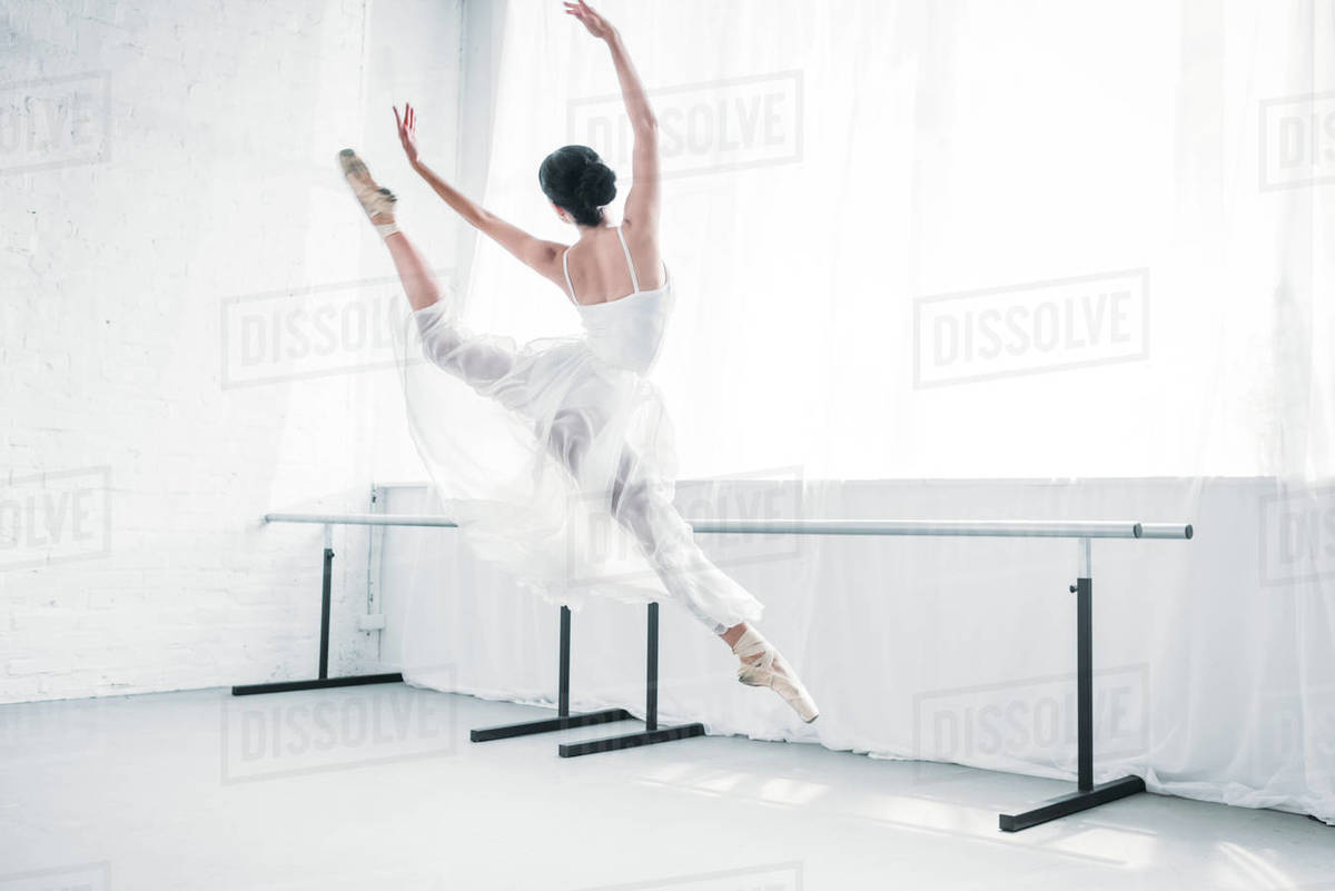 Back view of graceful young ballerina in white dress dancing in ballet ...