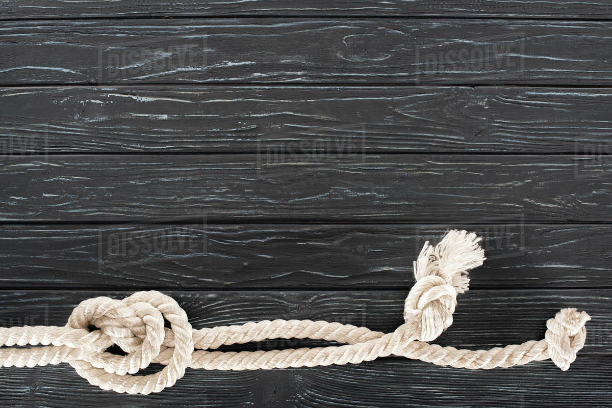 Top view of white nautical rope with knots on dark wooden tabletop ...