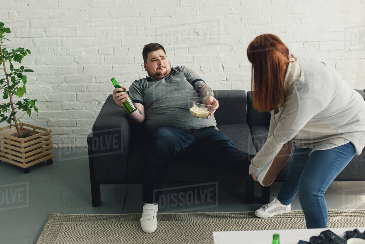 Size plus girlfriend holding boyfriend leg and pulling him from sofa at ...