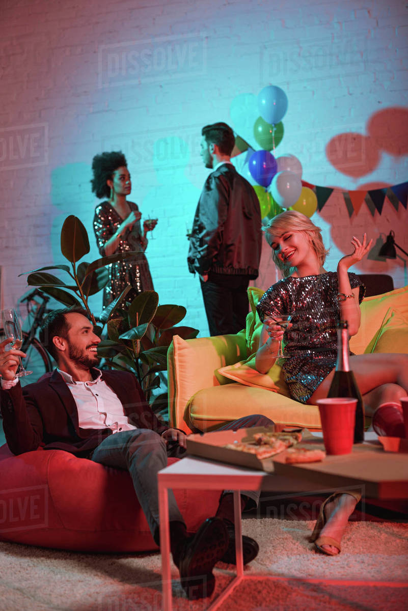 Smiling young people enjoying drinks and talking at party - Royalty ...