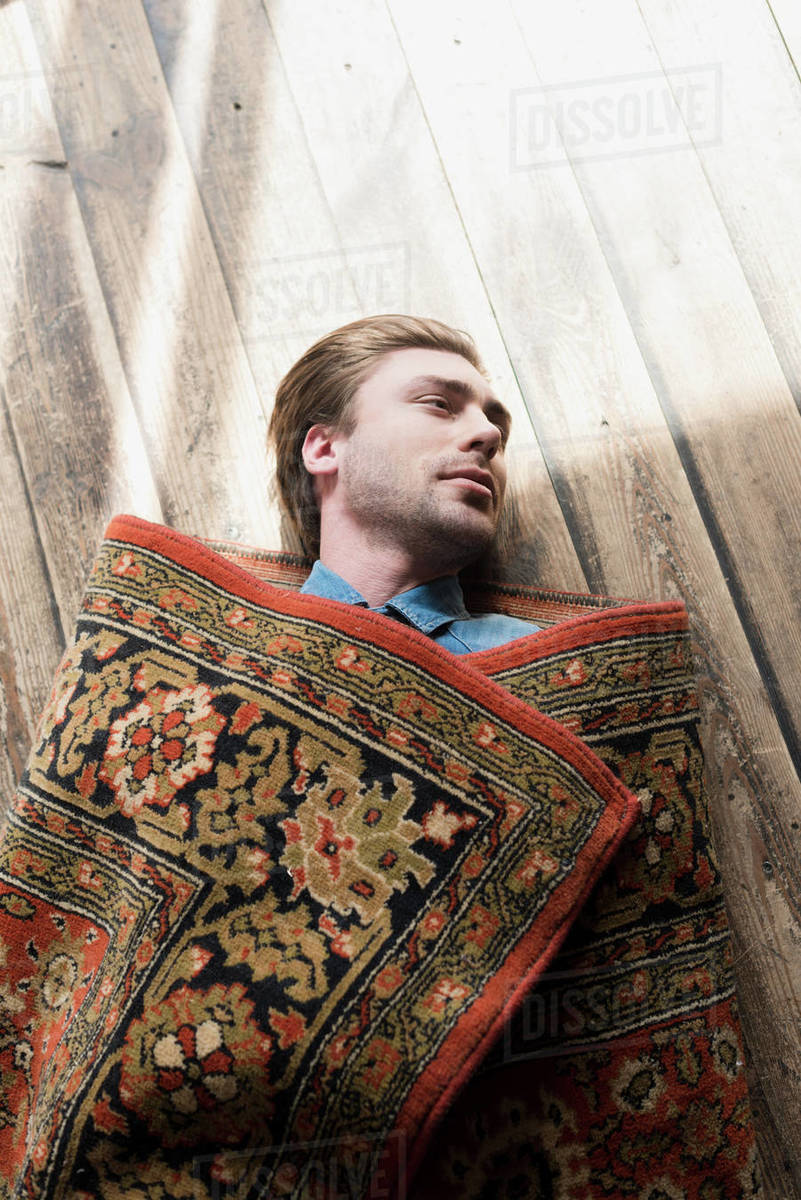 Top view of young man covered in rug lying on wooden floor - Royalty ...
