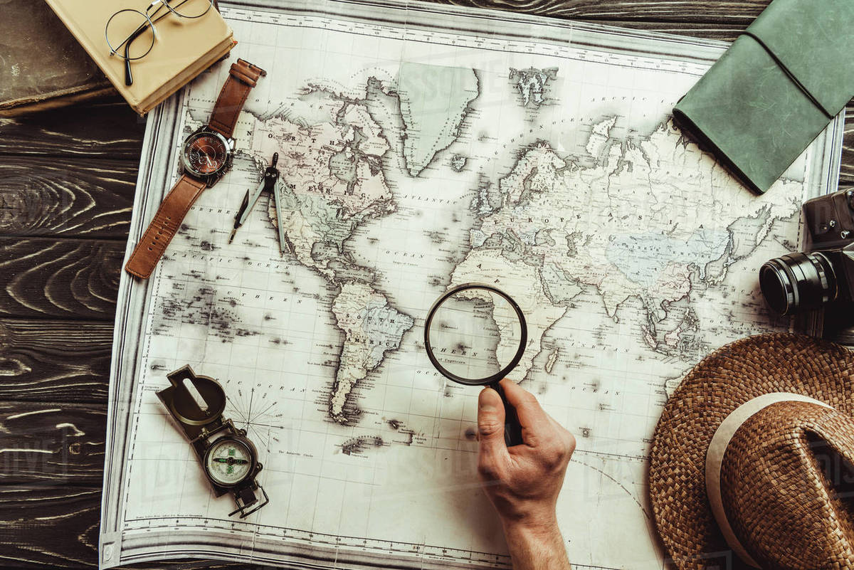 Cropped shot of man with magnifying glass at wooden tabletop with map ...