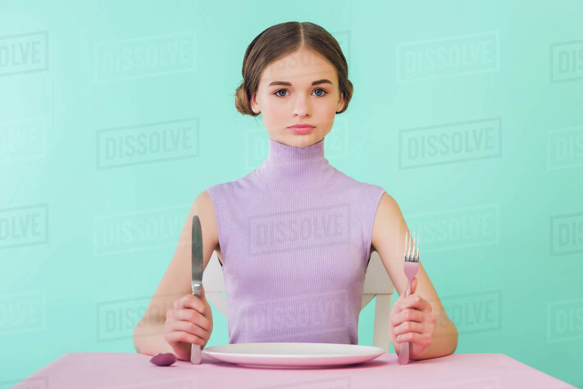 beautiful teen girl with knife, fork and empty plate sitting at table ...