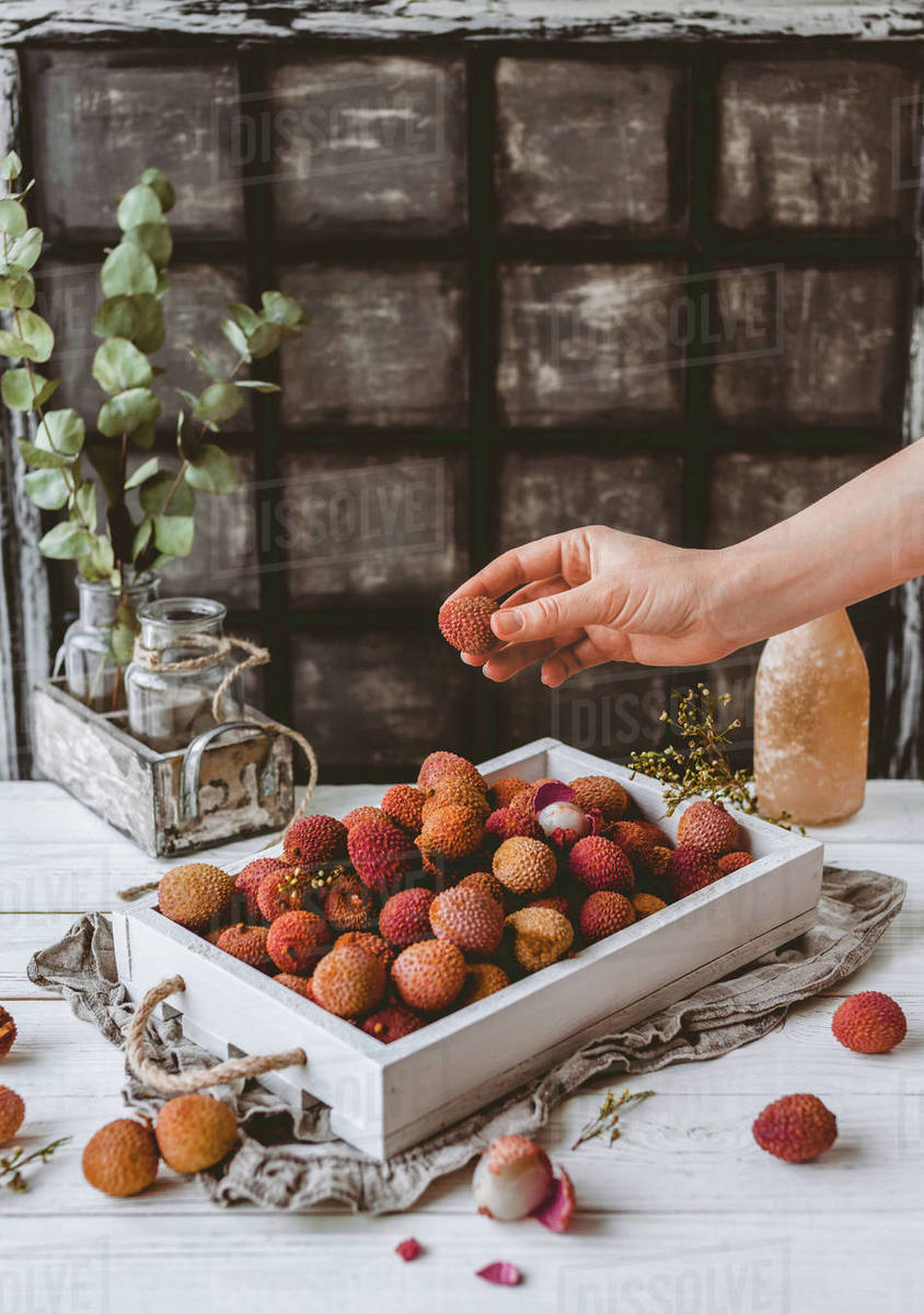 cropped image of female hand and pile of lychees in wooden box on table ...