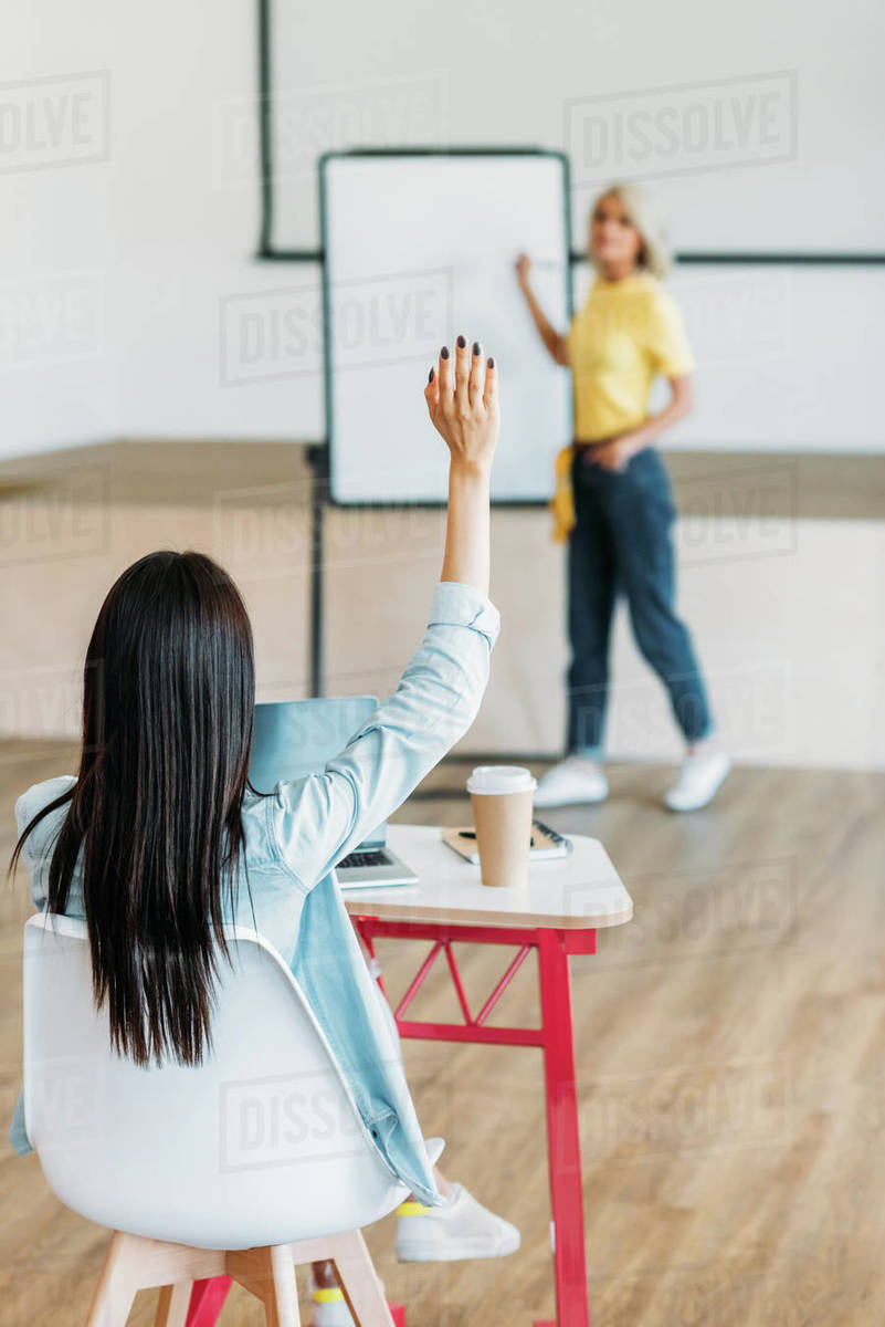 Rear view of student raising hand to answer at question of teacher ...