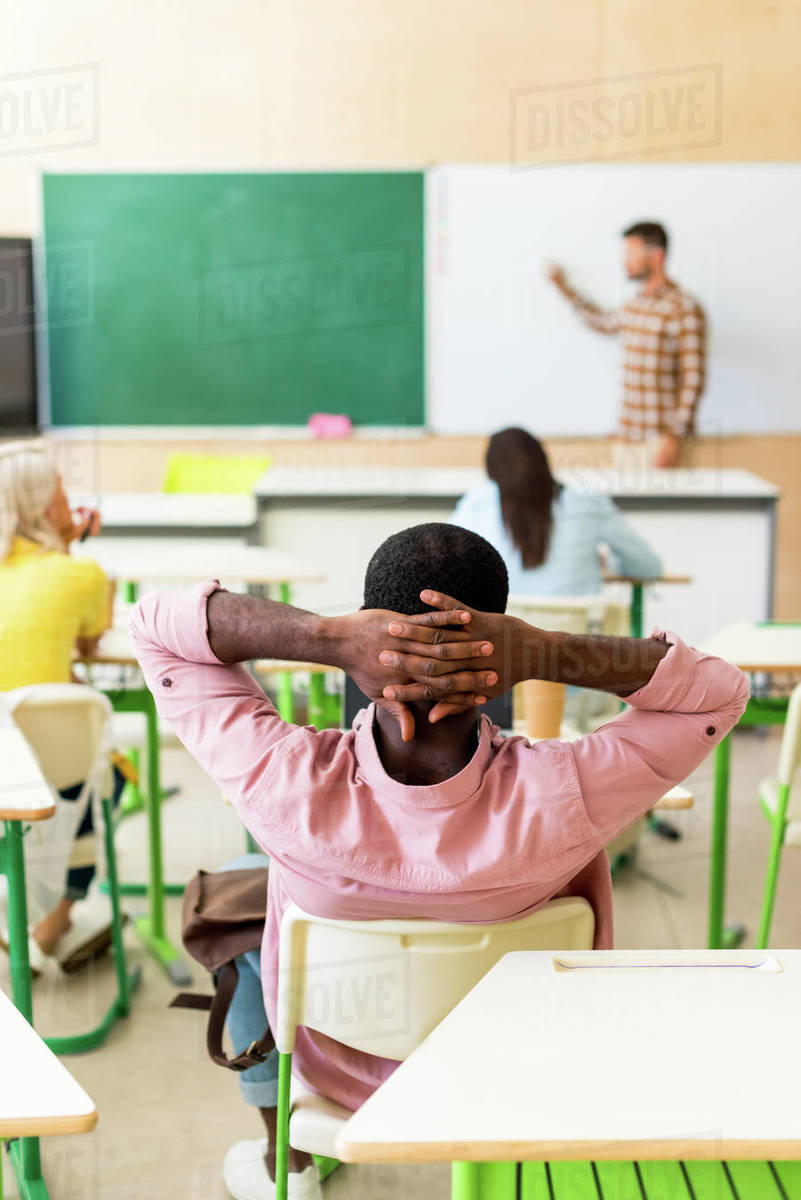 Rear view of relaxed african american student sitting at classroom ...