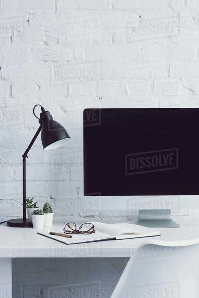 Computer with blank screen and glasses on notebook on table in modern ...