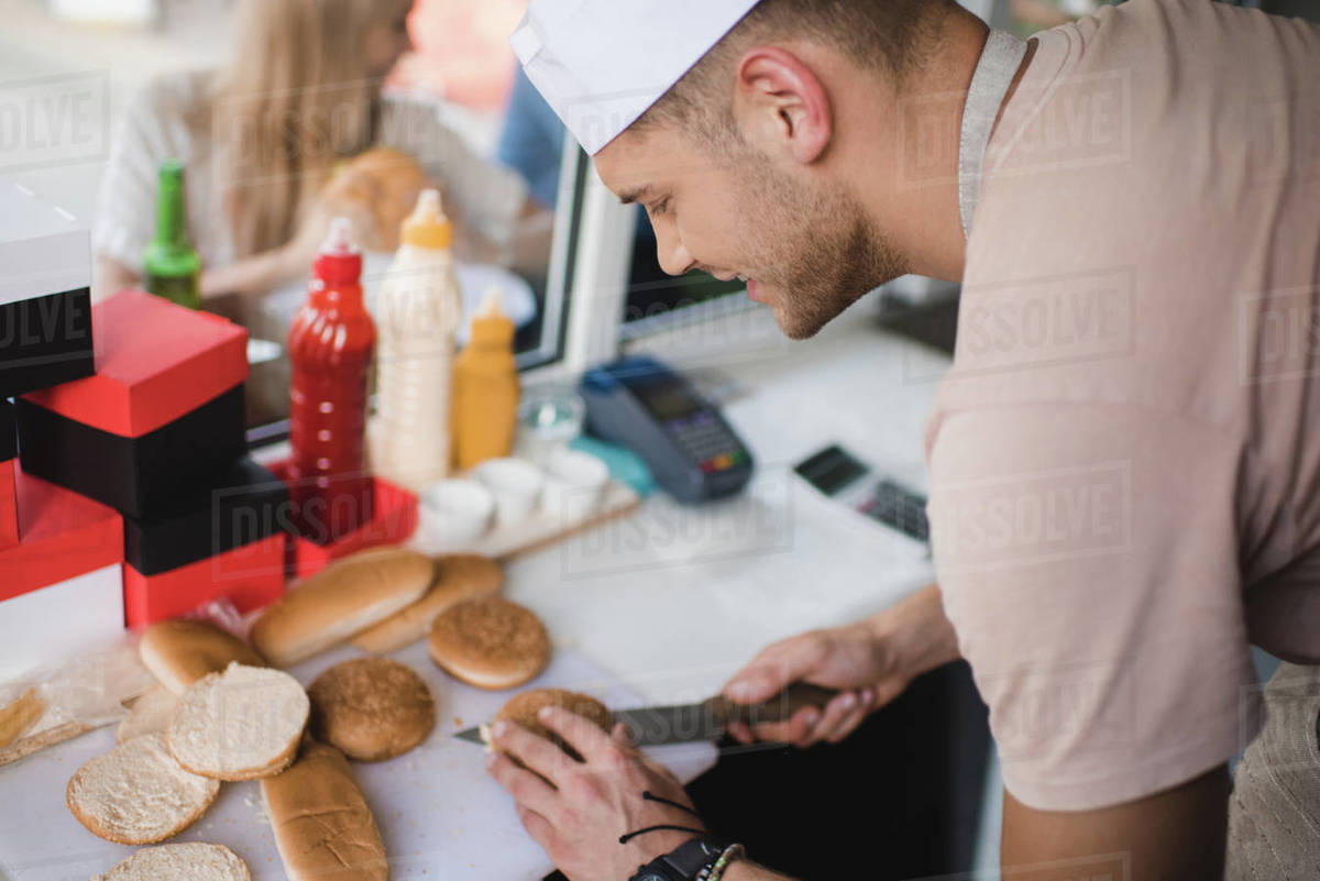Side view of chef cutting bun with knife in food truck - Royalty-free ...
