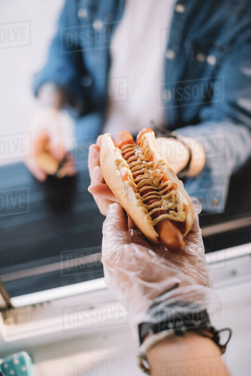 Cropped image of chef giving tasty hot dog to customer in food truck ...