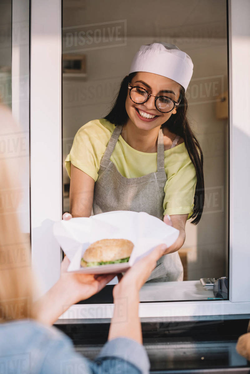 Cropped image of smiling chef giving burger to customer in food truck ...
