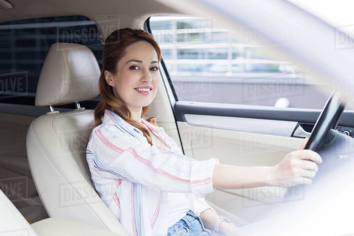 Side view of smiling woman looking at camera while driving car ...