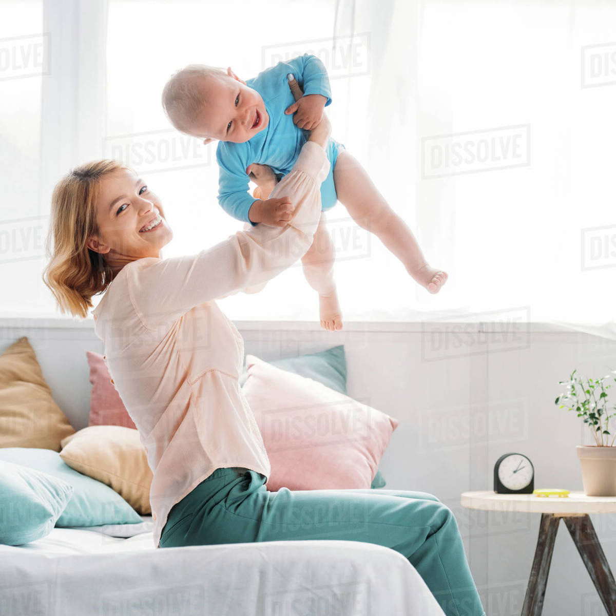 Happy mother raising up laughing little child while sitting on bed at ...