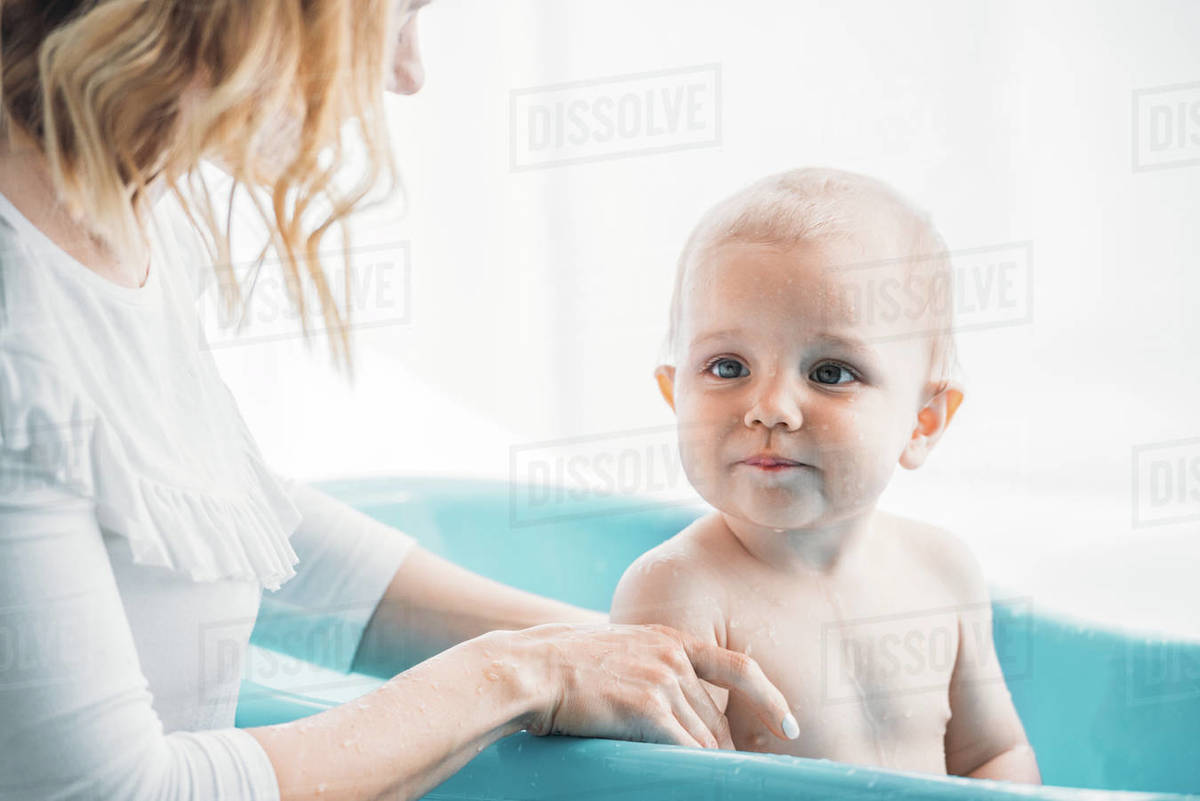 Mother washing her adorable little child in plastic baby bathtub at ...