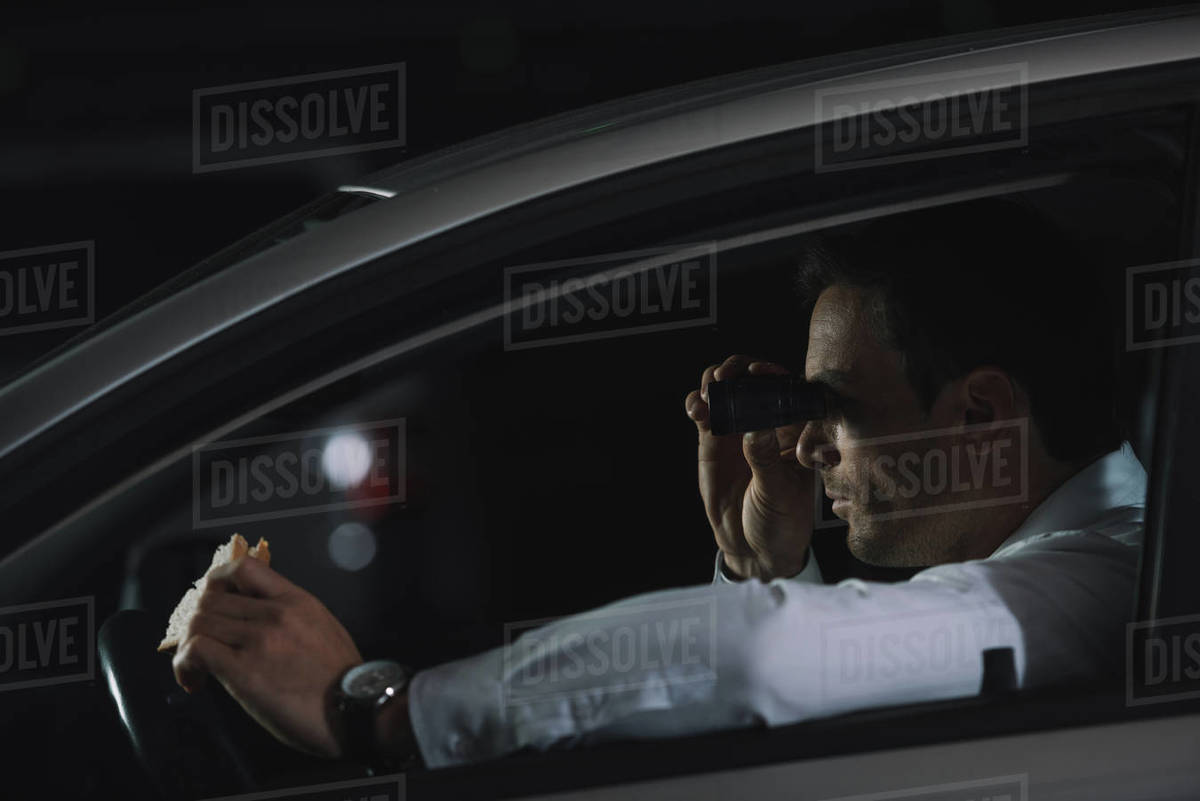 Side view of undercover male agent doing surveillance by binoculars and ...