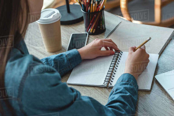 Cropped shot of girl taking notes in notebook while studying at home ...