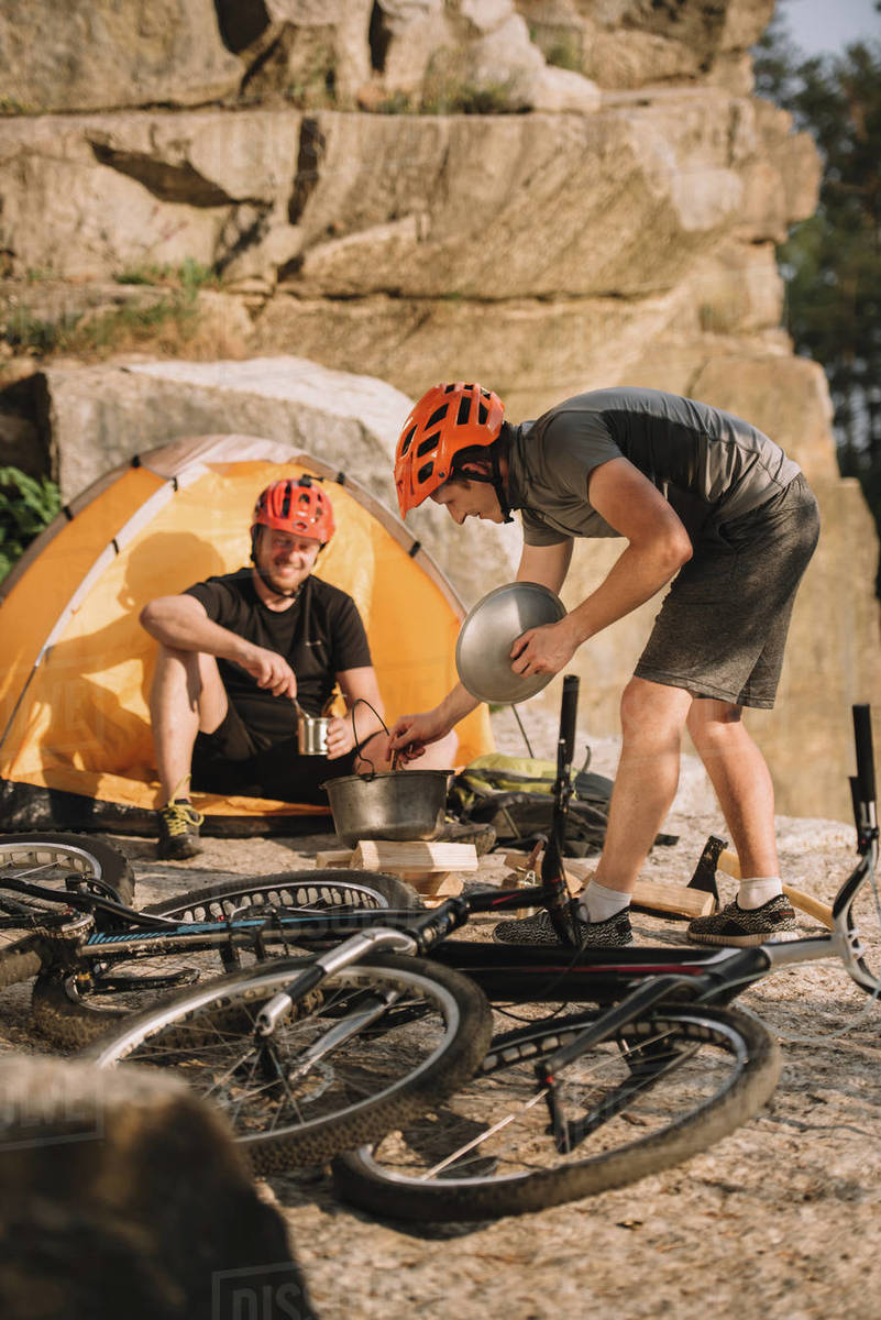 Young trial bikers cooking food on camping outdoors - Stock Photo ...