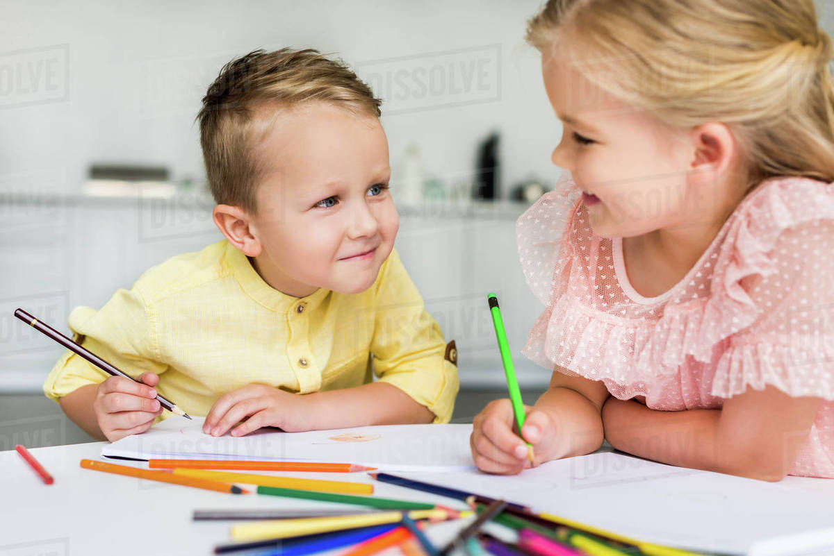 Adorable kids smiling each other while drawing with colored pencils ...
