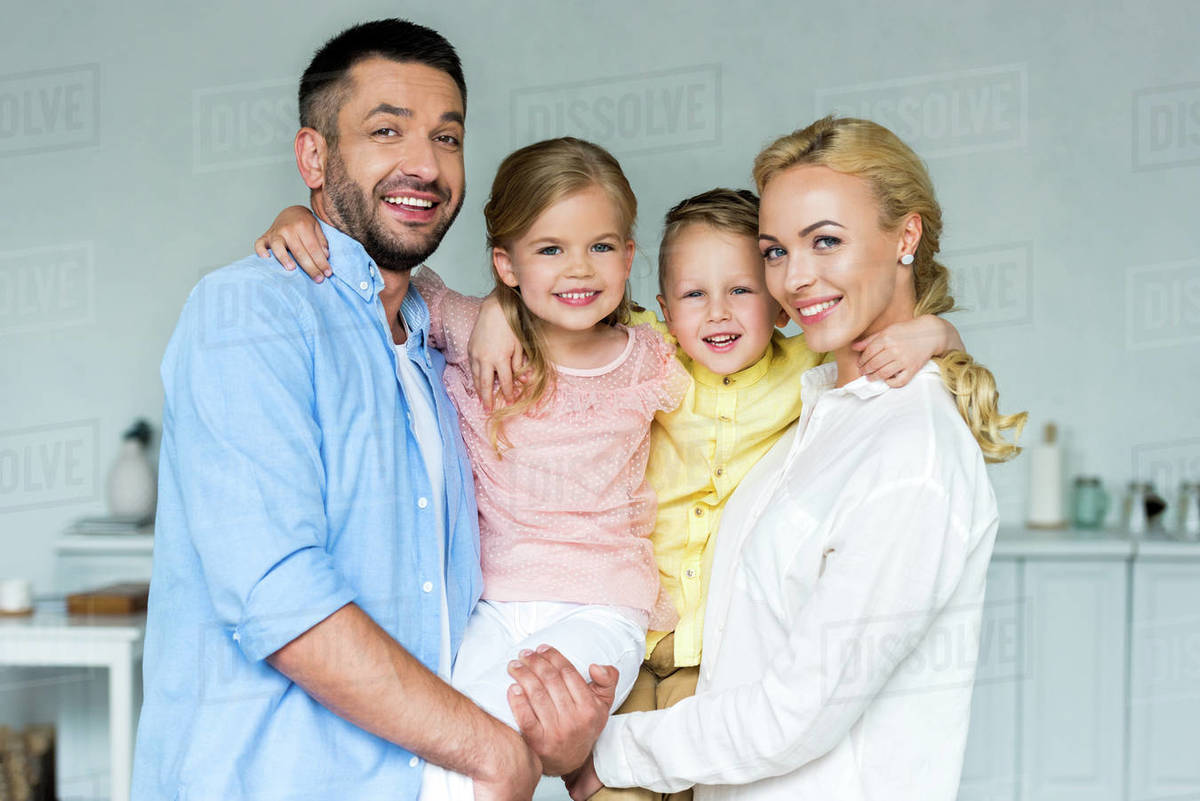 Happy family with two adorable children smiling at camera together at ...