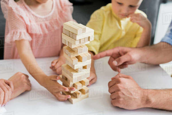 Cropped shot of family with two children building tower from wooden ...
