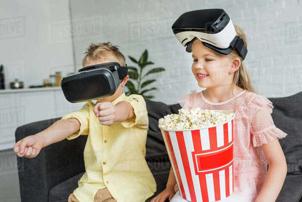 Adorable kids using virtual reality headsets and eating popcorn at home ...