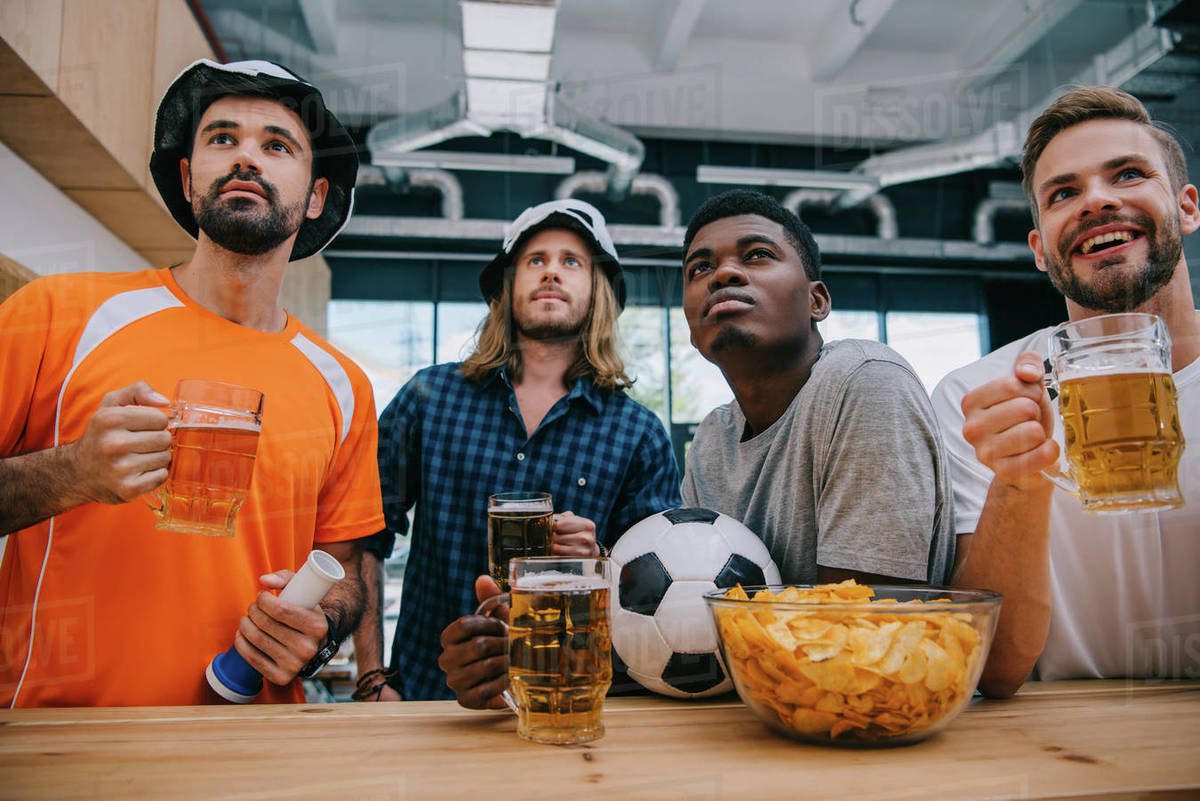 Concentrated multicultural group of male football fans with beer ...
