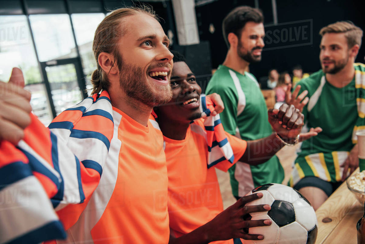 Excited multicultural football fans in orange t-shirts and scarf ...