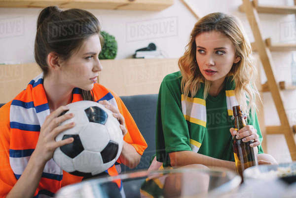 Two female football fans in different fan t-shirts with ball and beer ...