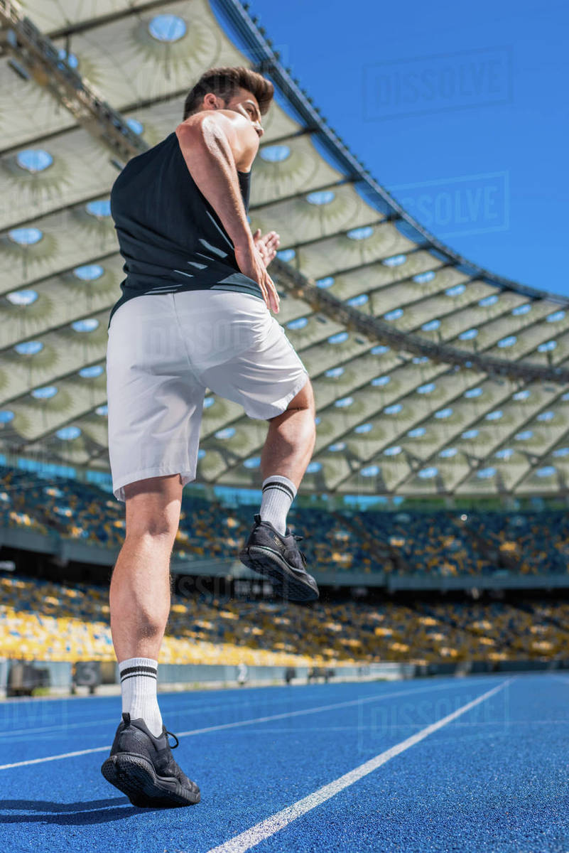 Rear view of athletic young man exercising on running track at sports ...