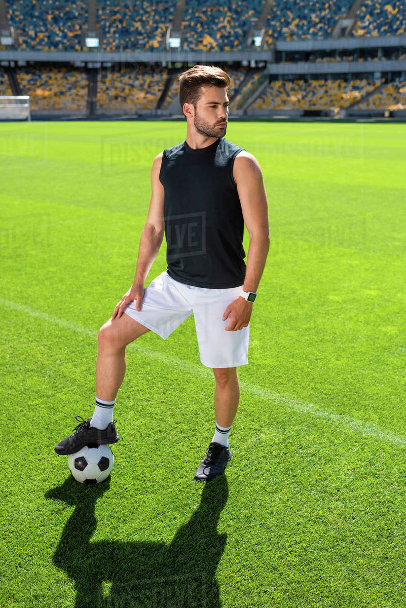Serious young soccer player standing at sports stadium with ball ...