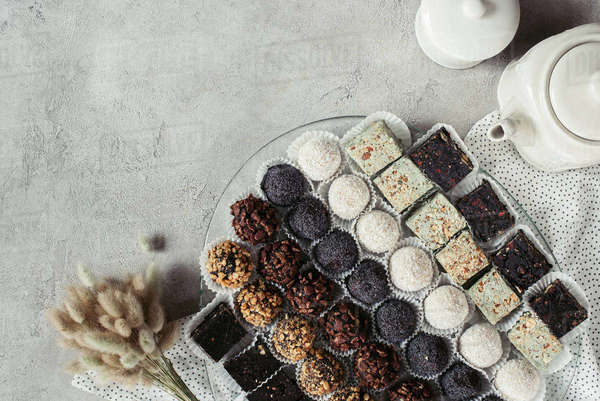 Flat lay with various sweet desserts on plate, teapot and linen on grey ...