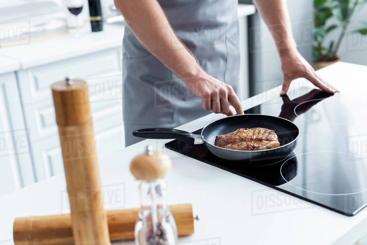 cropped shot of man cooking delicious steak in frying pan on stove ...