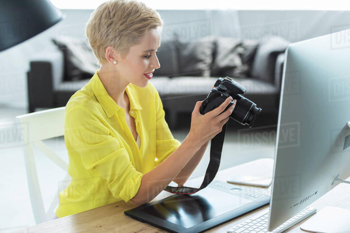 side view of female photographer looking at camera screen at table with ...