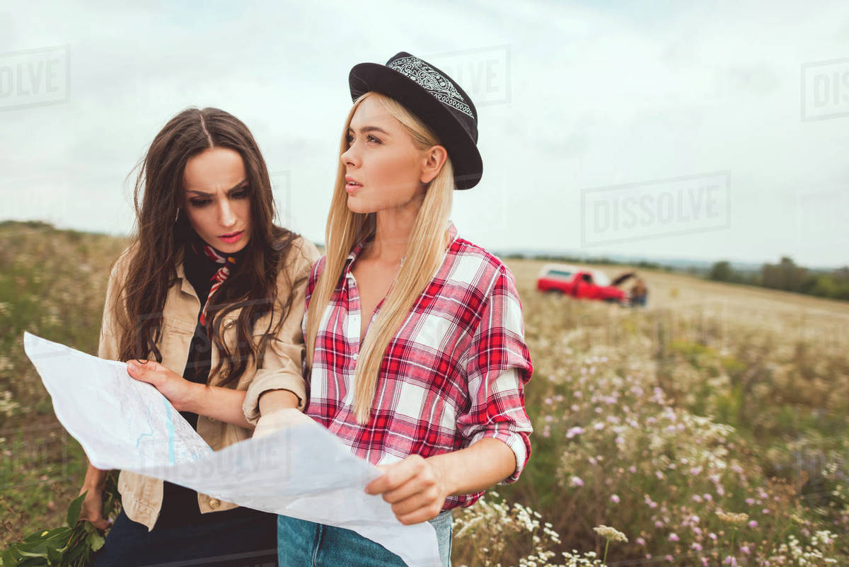 confused young girlfriends with map standing in field and trying to ...