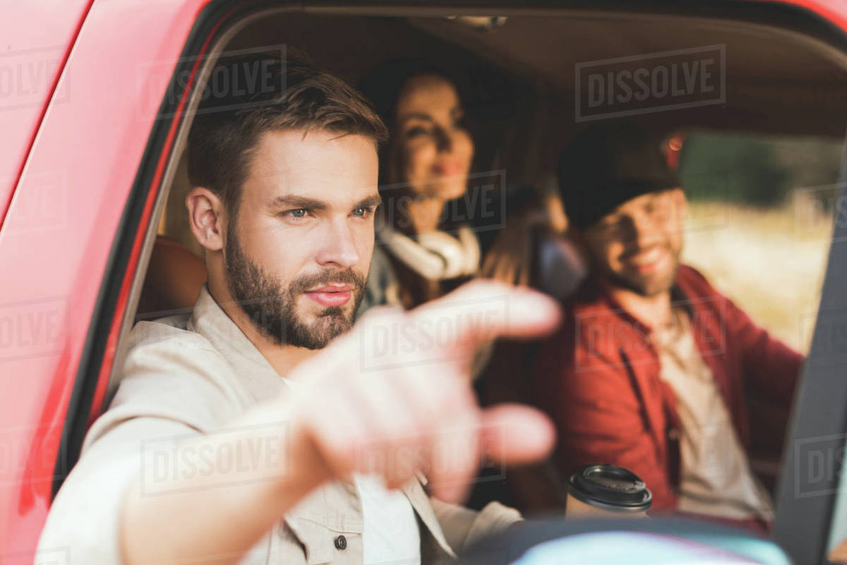 handsome young man pointing somewhere while riding car with friends ...