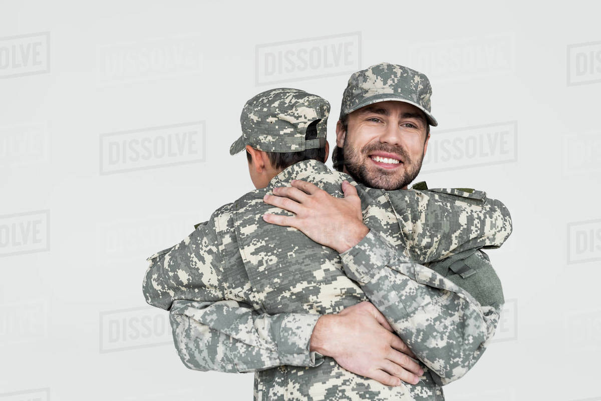 partial view of smiling soldier and son in military uniforms hugging ...