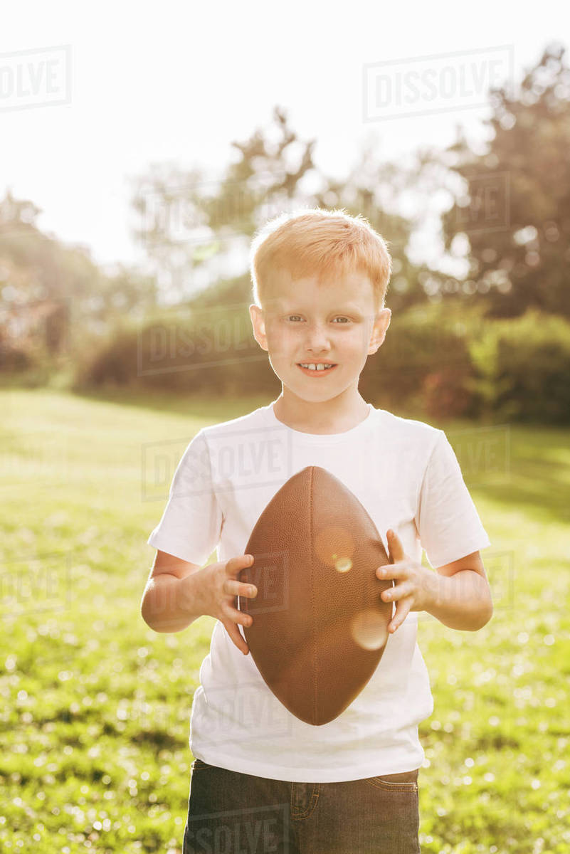 adorable child holding rugby ball and smiling at camera in park - Stock ...