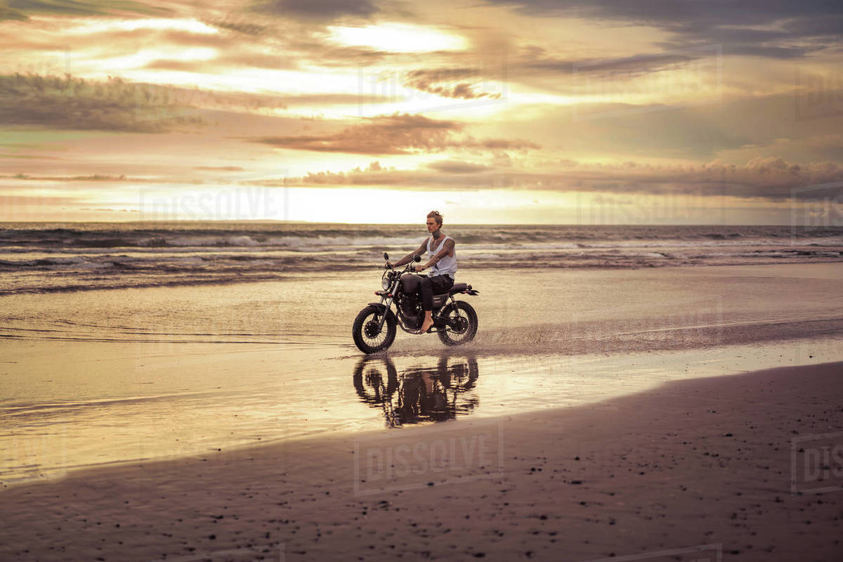 tattooed biker riding motorcycle on ocean beach during sunset - Royalty ...