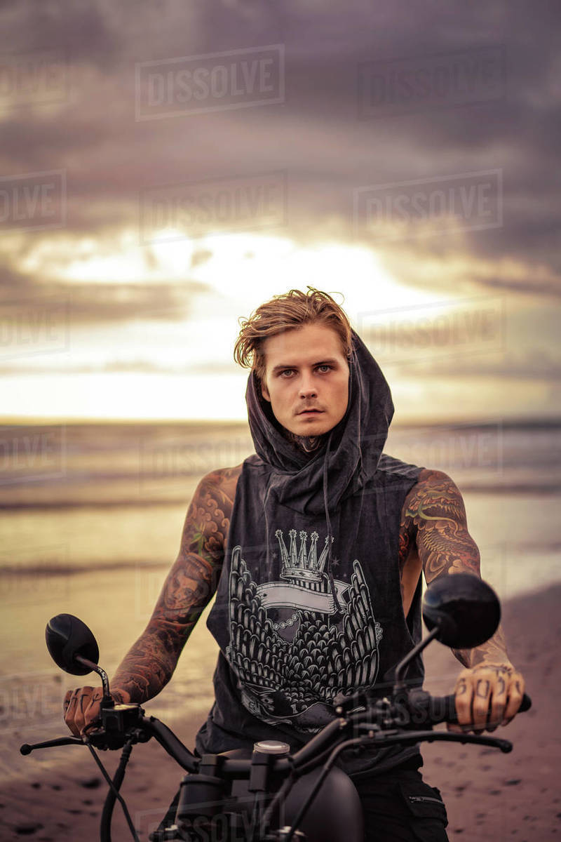 handsome tattooed biker with motorcycle on ocean beach looking at ...