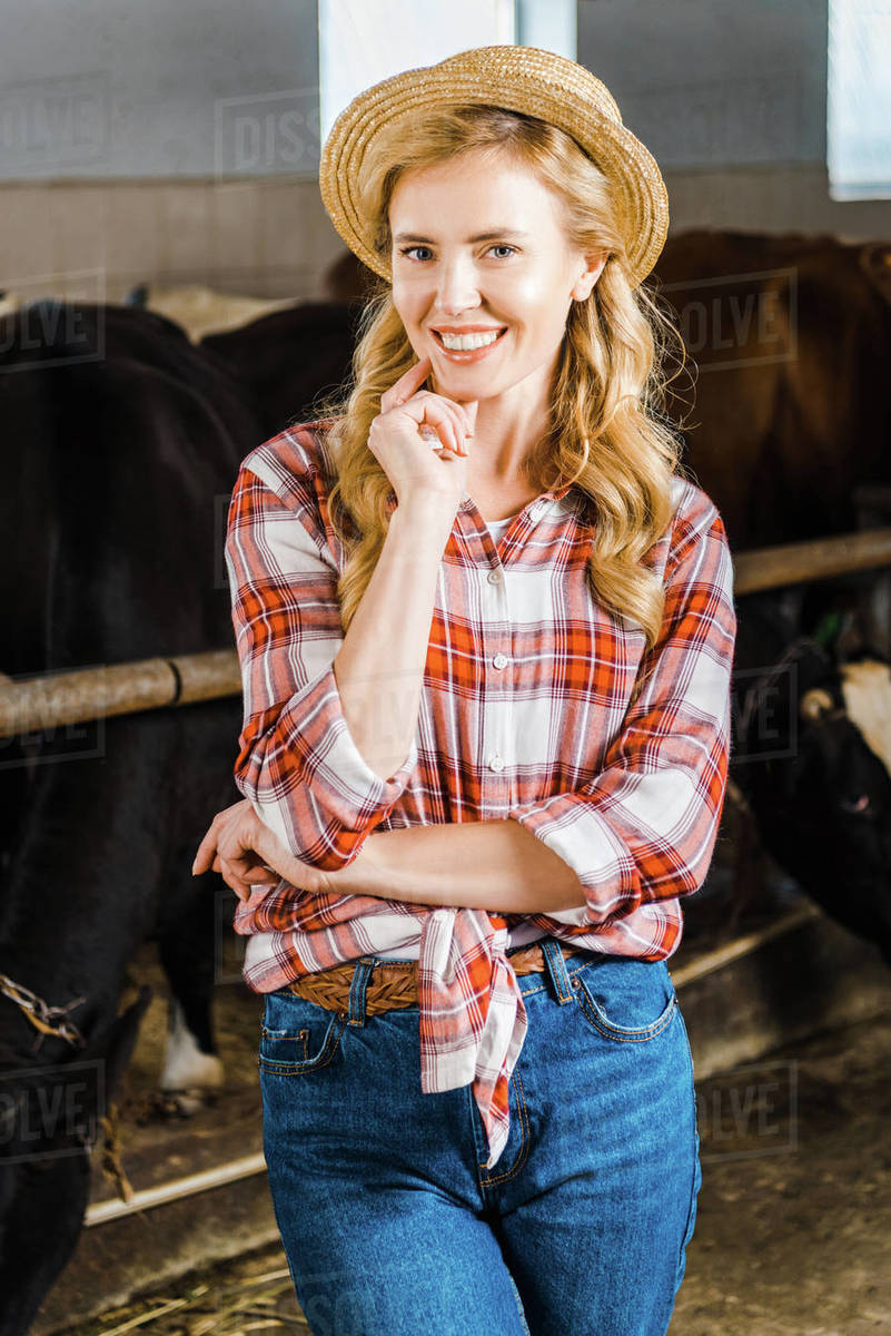 Portrait of attractive farmer in straw hat looking at camera in stable ...